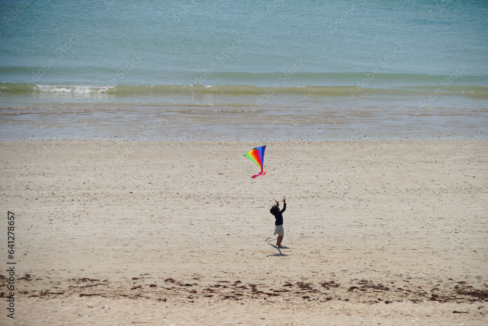 Une petite fille joue avec un cerf-volant qui vole sur une plage Stock ...
