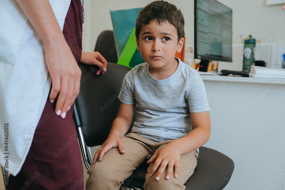 Sad frightened little boy sitting at medical office on chair looks ...