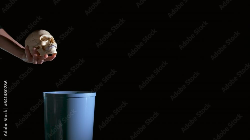 Throw human skull. A woman hands with skull put it into the waste bin ...