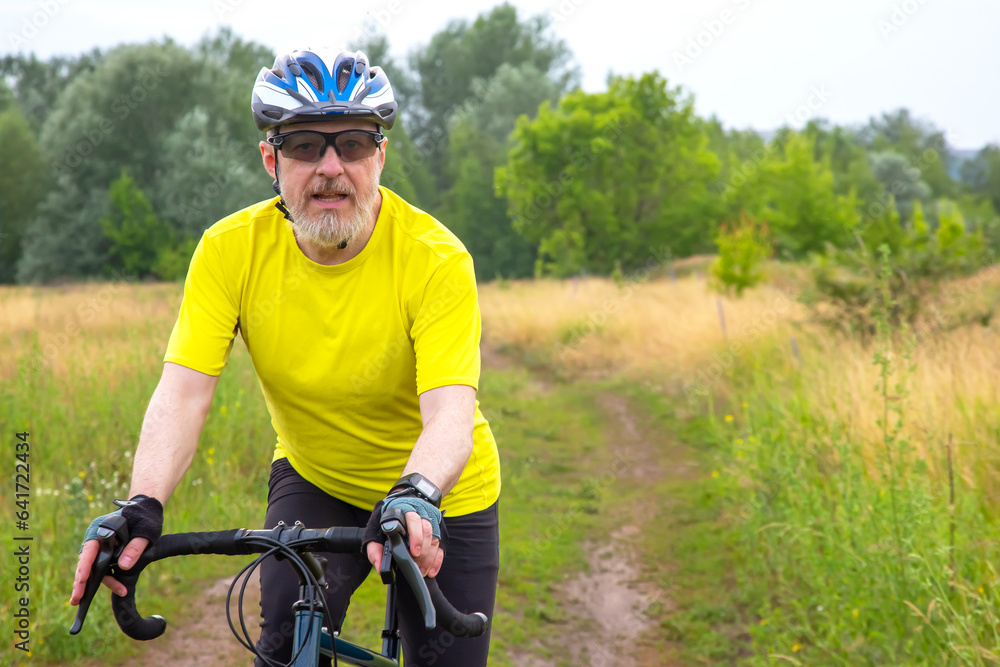 bearded man cyclist in yellow clothes rides a bike on a road in nature ...