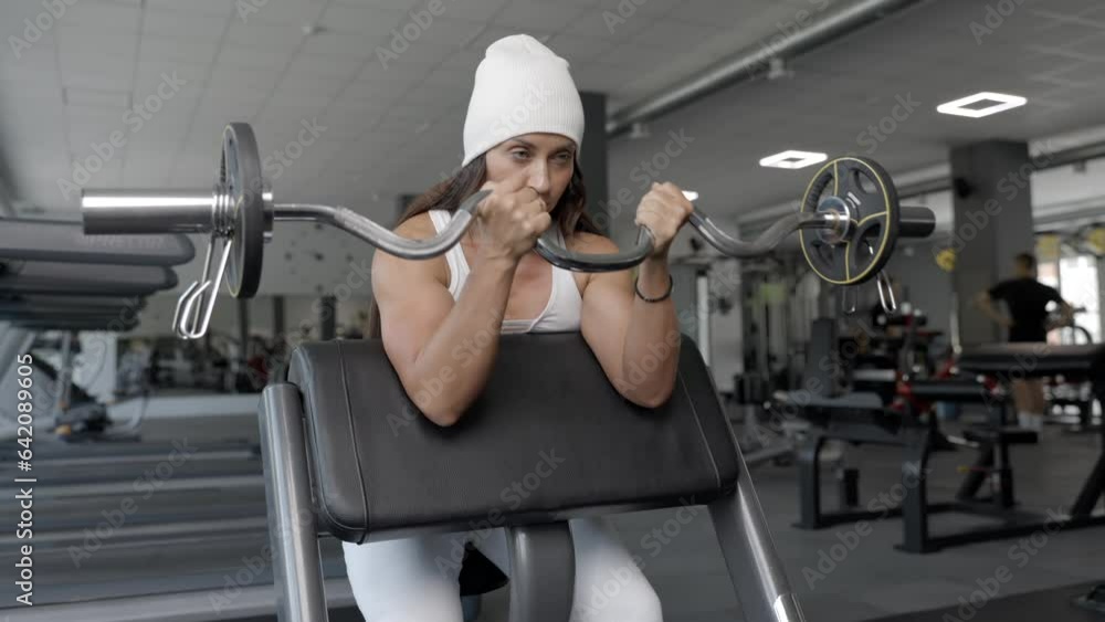 A young woman does exercises for biceps with a barbell with a curved ...