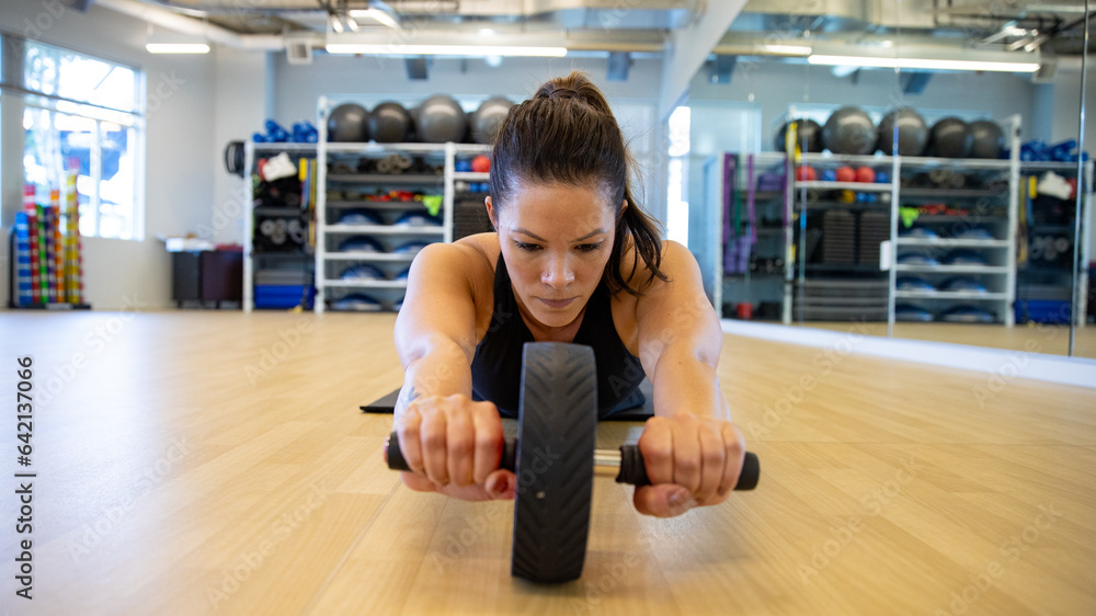 Strong woman exercising in the gym with an ab roller. She is working ...