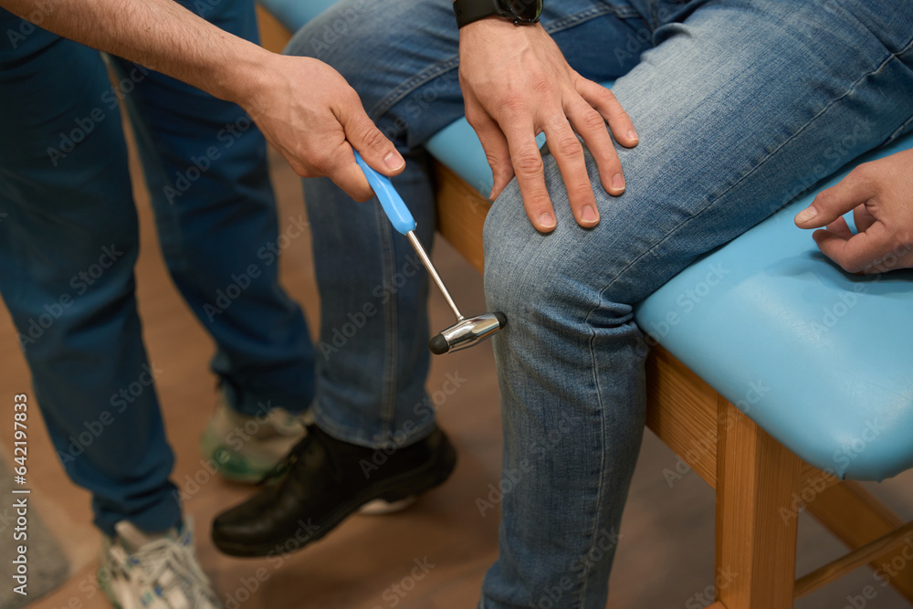 Experienced doctor checking patellar reflex in man during neurological ...
