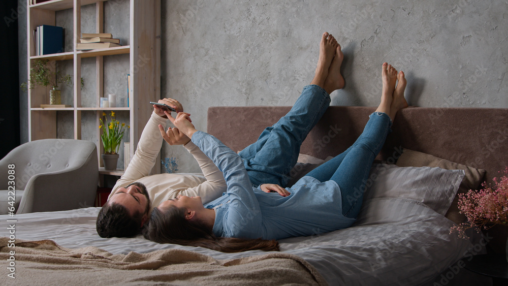 Carefree Caucasian couple in love lying down kick up feet on bed family ...