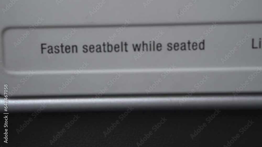 Fasten seatbelt while seated sign on the back of a seat on an airplane ...