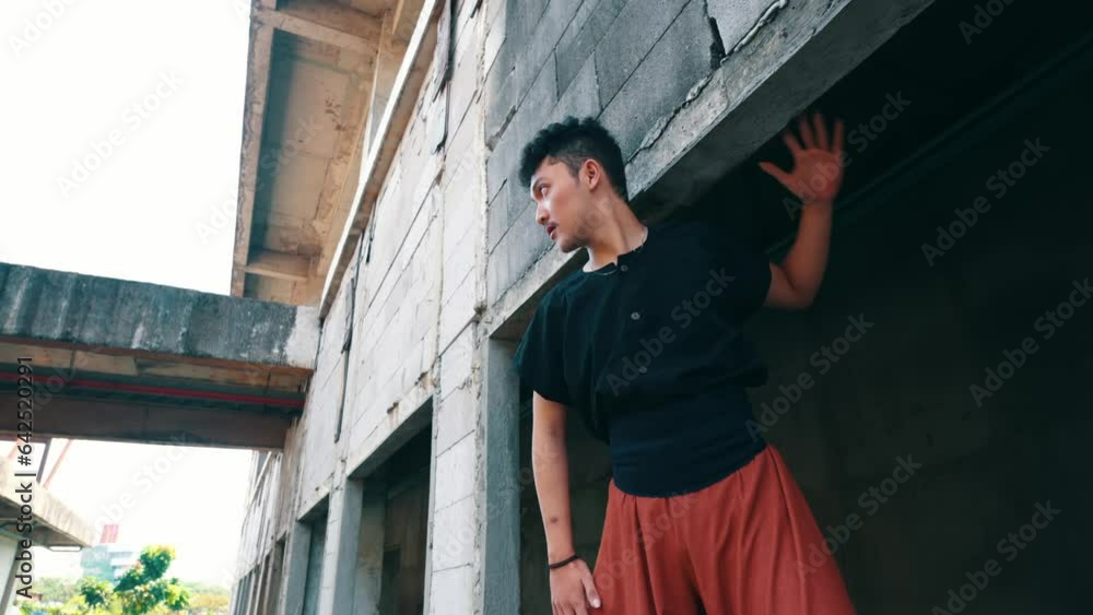 an Asian man standing and leaning on a concrete wall with a sad face ...