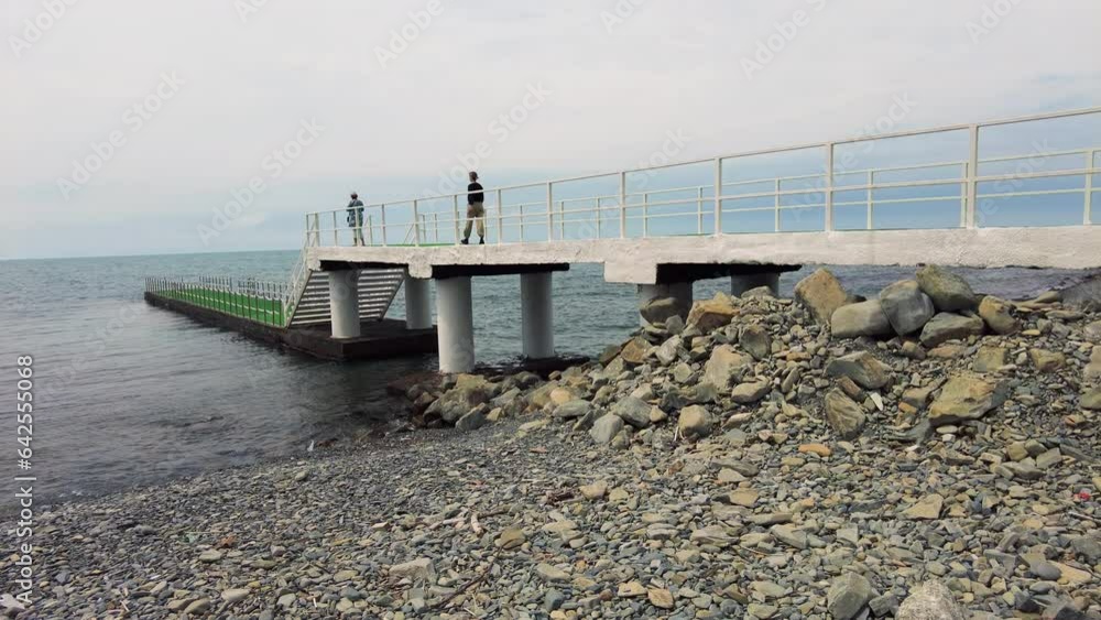 Women walk along the pier stretching into the Black Sea. Russia, Abrau ...