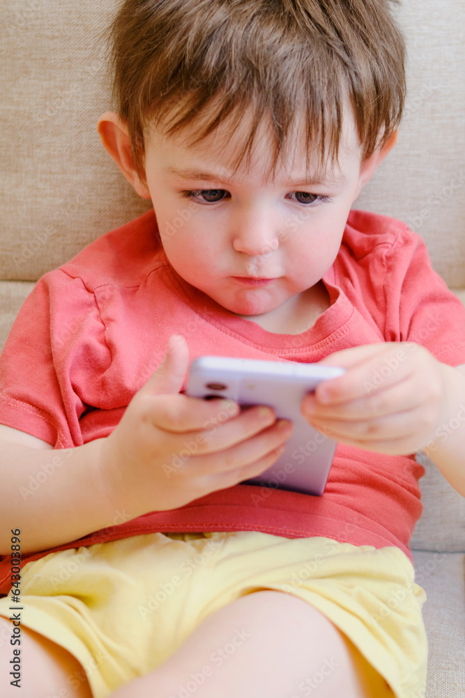Toddler is busy tapping the phone screen. The phone-holding child looks ...