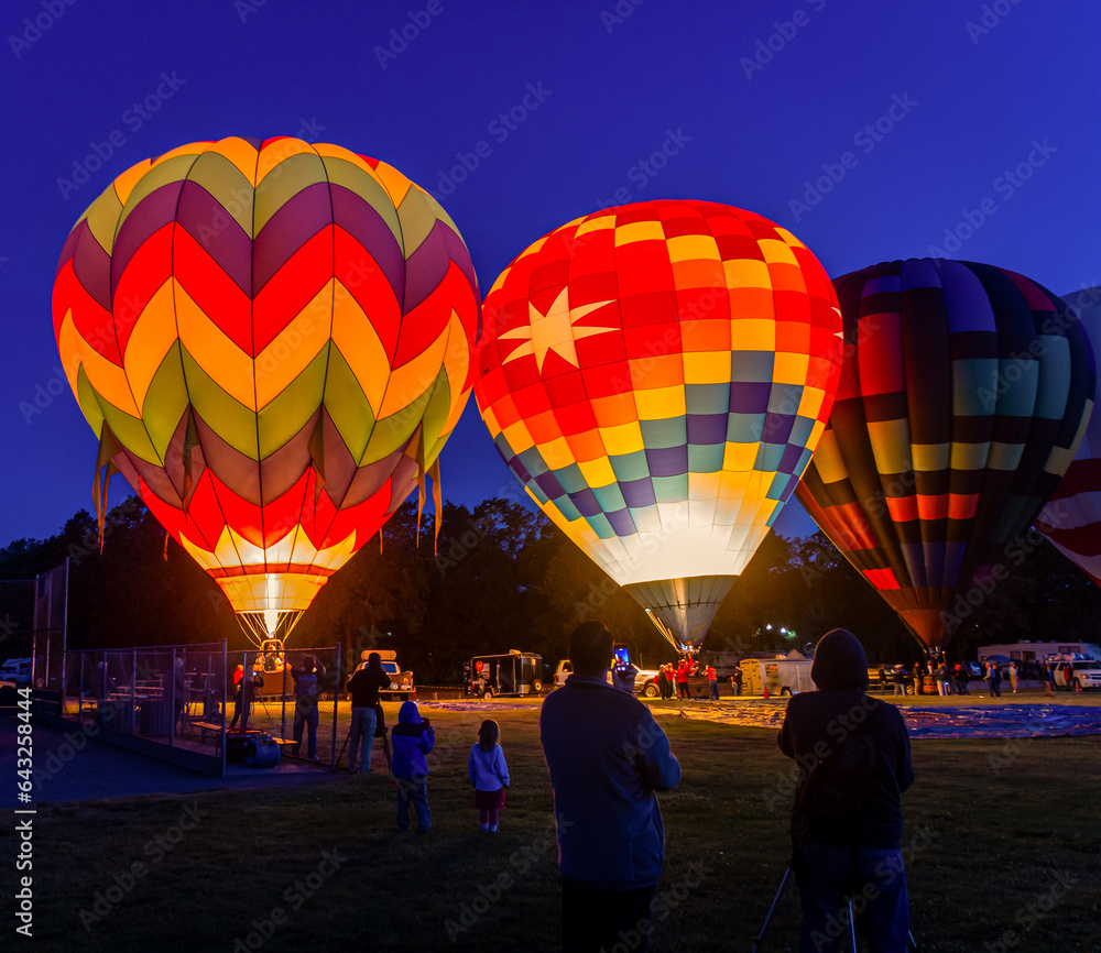 Two hot air balloons are lit up in an early dawn. The gas flame is ...