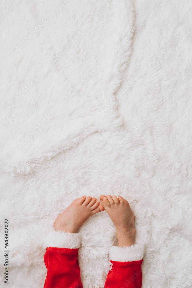 The bare feet of a child dressed as Santa on a white fluffy background ...
