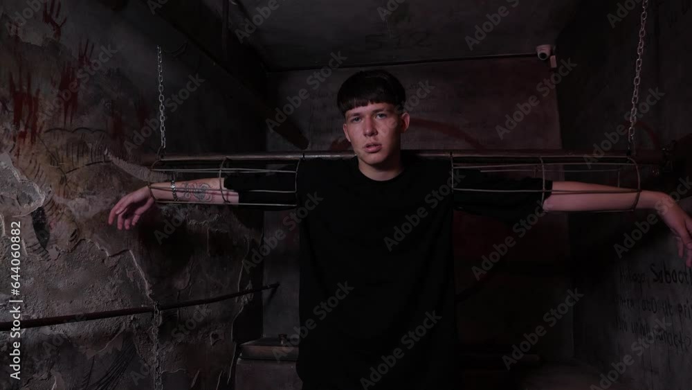 A young man is chained to horizontal handcuffs in a dark quest room. A ...