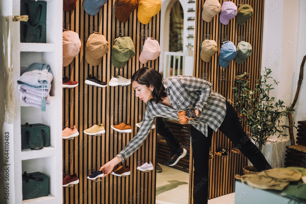 Saleswoman bending over while arranging shoes on display rack at ...