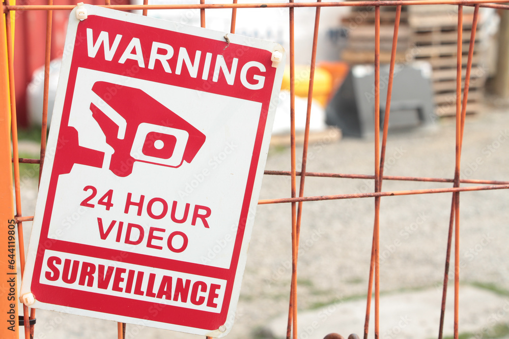 warning 24 hour video surveillance sign on orange locked gate for dirt ...
