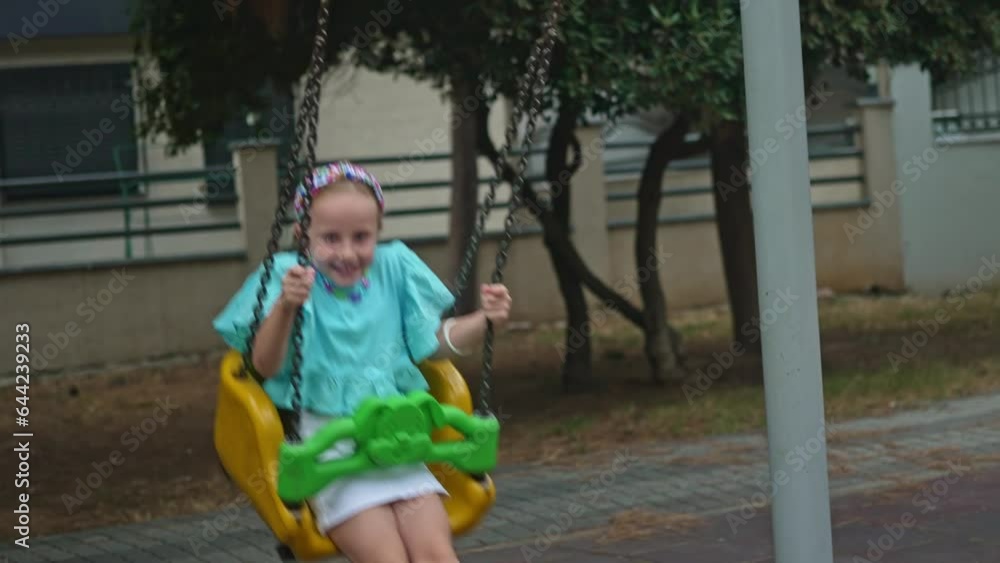Cheerful little girl in fancy blouse rides swings with chains in urban ...