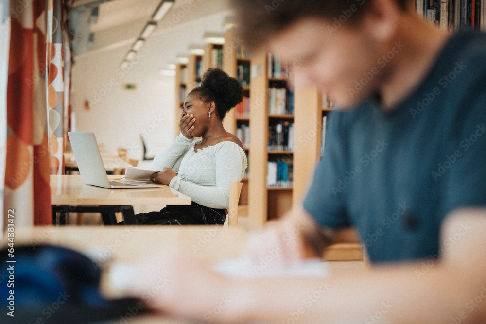 Student yawning while studying in library at university Stock Photo ...