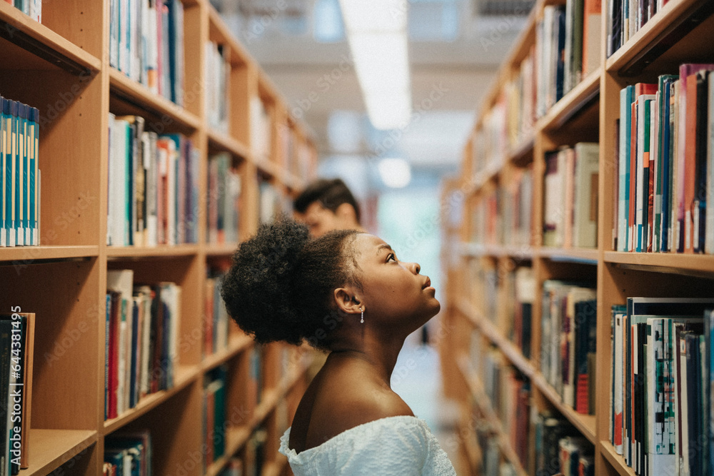 Side view of student searching books on bookshelf in library at ...