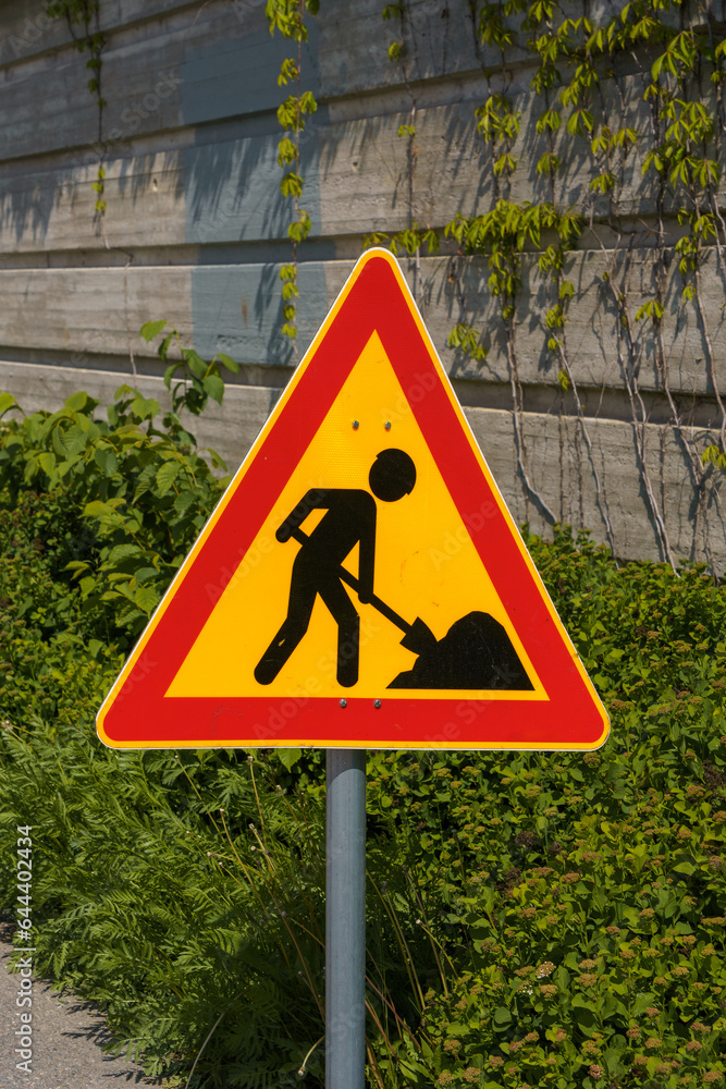 Roadworks warning sign with green bushes and a concrete wall in the ...