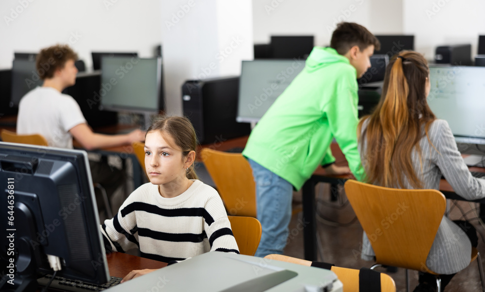 Poster Portrait of interested tween girl during lesson in computer room ...