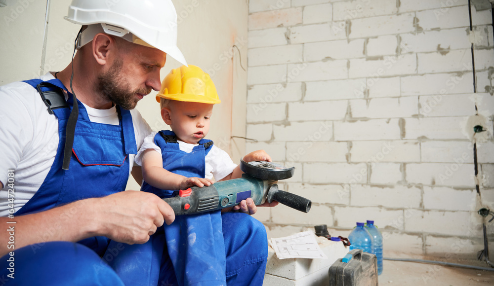 Little boy sitting on father lap and holding electric power grinding ...