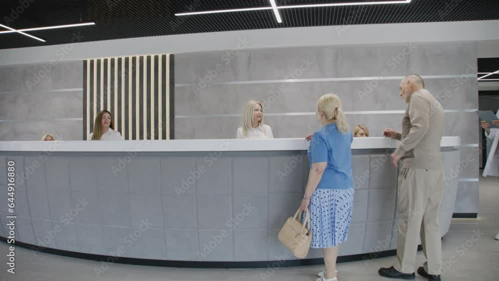 Elderly couple come to reception desk in clinic waiting room and make ...