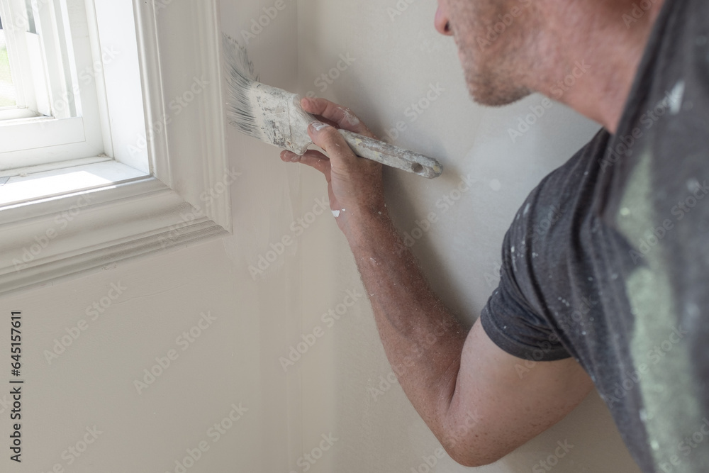 Painter painting the wall in between the window frame and corner of ...