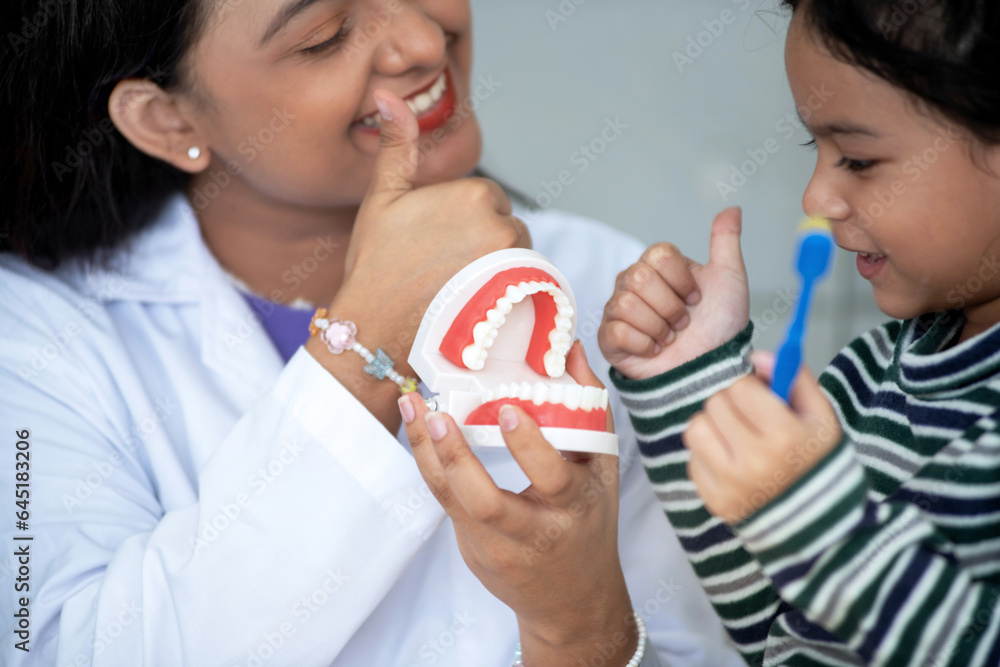 Dentist showing a jaw model to a little girl and suggest the correct ...