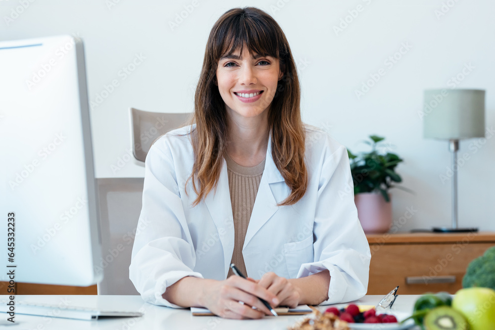 Beautiful smart nutritionist woman working with computer while looking at camera in the ...