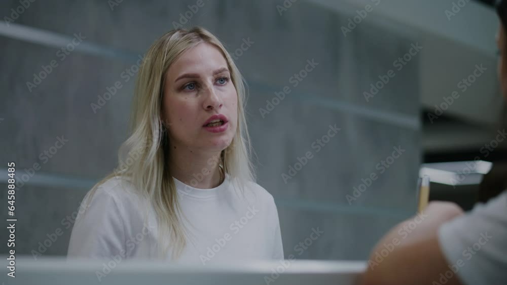 Female administrator speaks with patient at reception desk in clinic ...