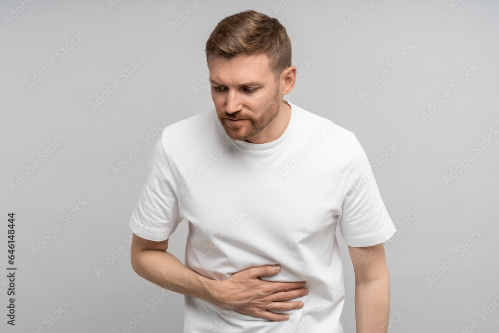 Sick man feeling pain in stomach holding abdomen on grey background ...