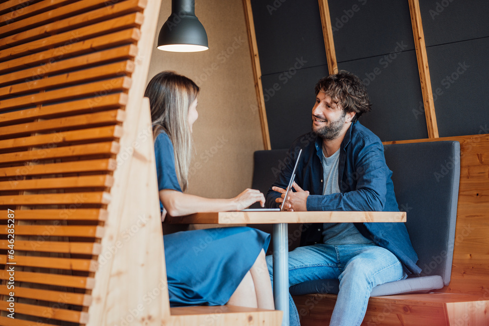 Smiling business people sitting talking in office cubicle using laptop ...