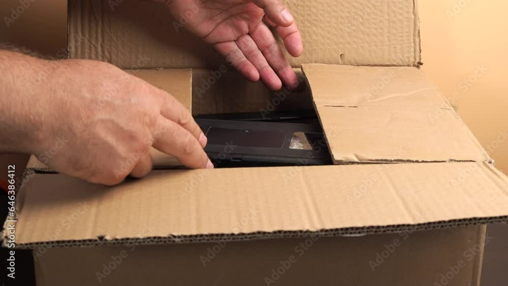 Old VHS tapes in a cardboard box. A man opens a cardboard box with VHS ...
