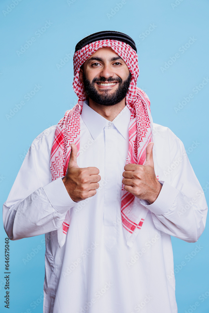 Smiling muslim man dressed in traditional islamic clothes showing two ...