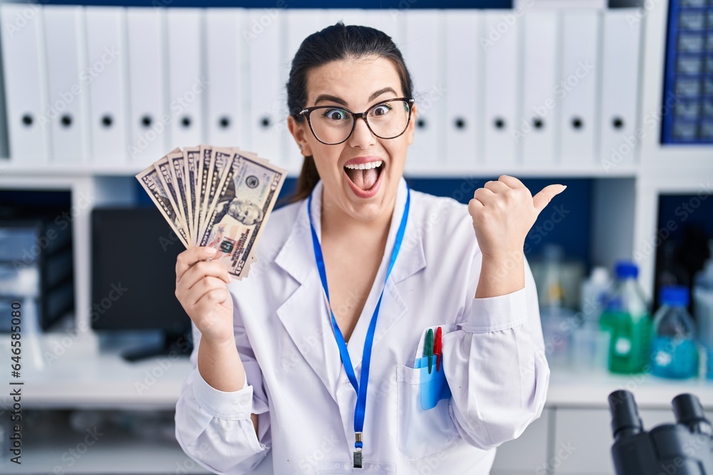 Young brunette woman working at scientist laboratory holding money ...
