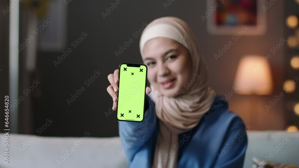 Smiling covered Muslim woman in hijab showing smartphone screen with ...