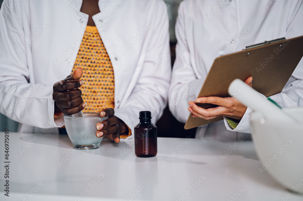 Cropped picture of the multiracial pharmacists making a cure and mixing ...