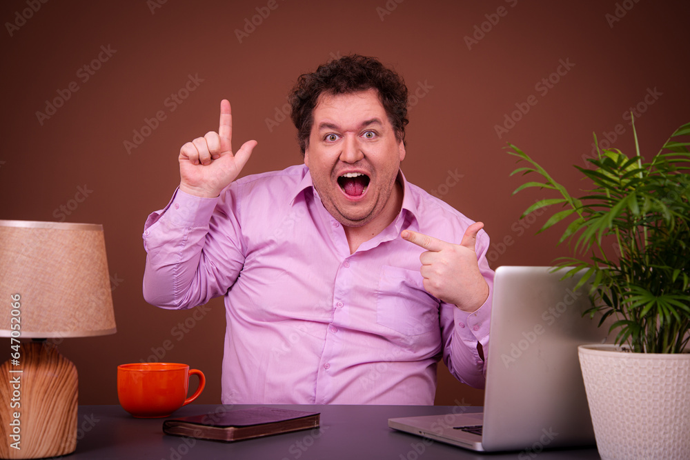 Funny fat man posing at a table with a laptop. Hard work online early ...
