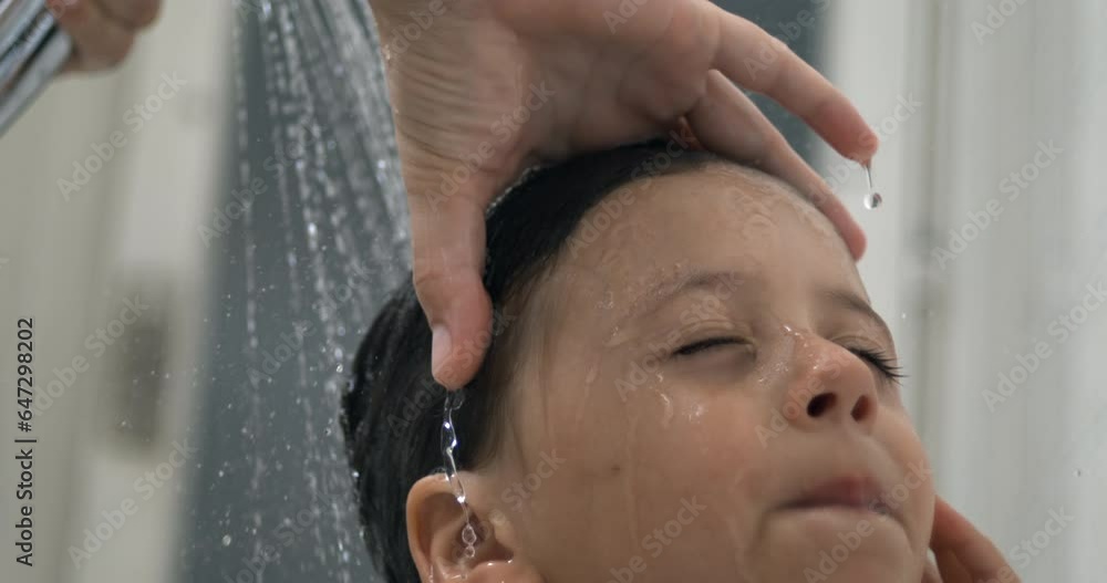 Close-up child face underneath flowing water shower head during bath ...