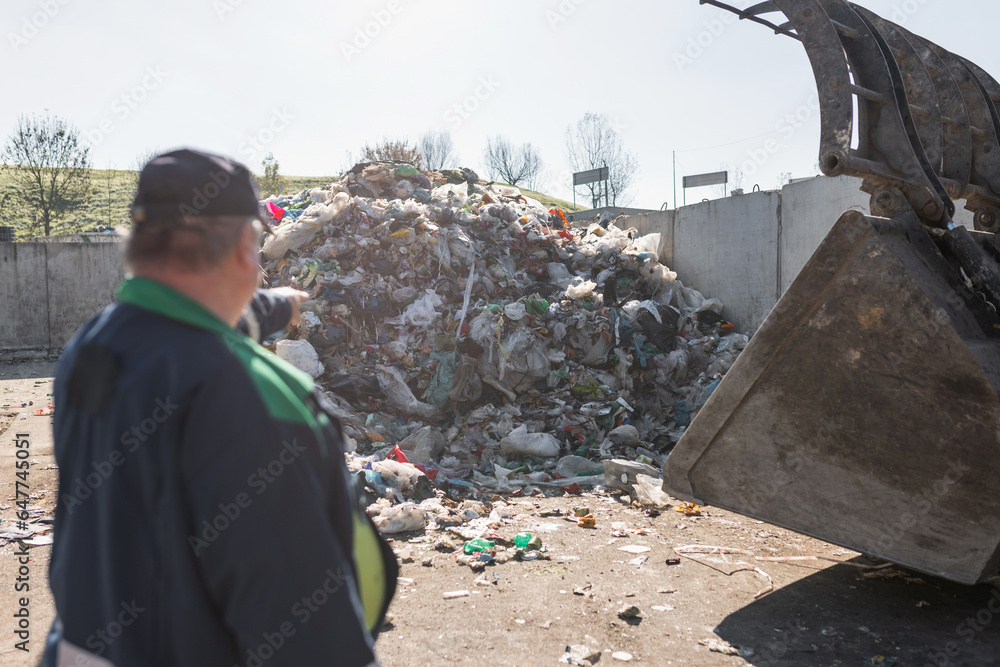 Landfill worker directing skid steer loader on the garbage heap. Waste ...