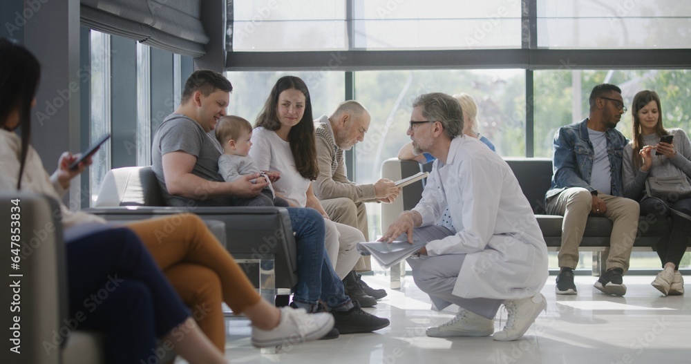 Diverse people sit on couches in clinic lobby area, wait for doctors ...