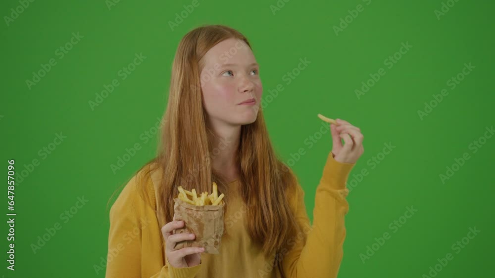 Green screen. Blonde teenage girl smiles and eats french fries. Modern ...