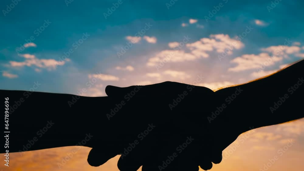 Silhouettes of man and woman are shaking hands against the sunrise or ...