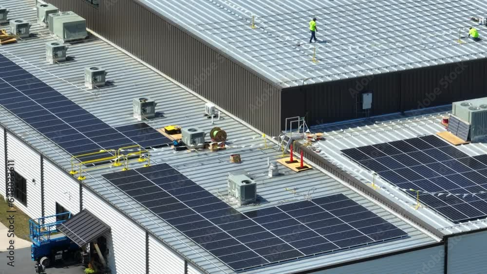 Industrial roof solar panel installation. Workers in neon on flat ...