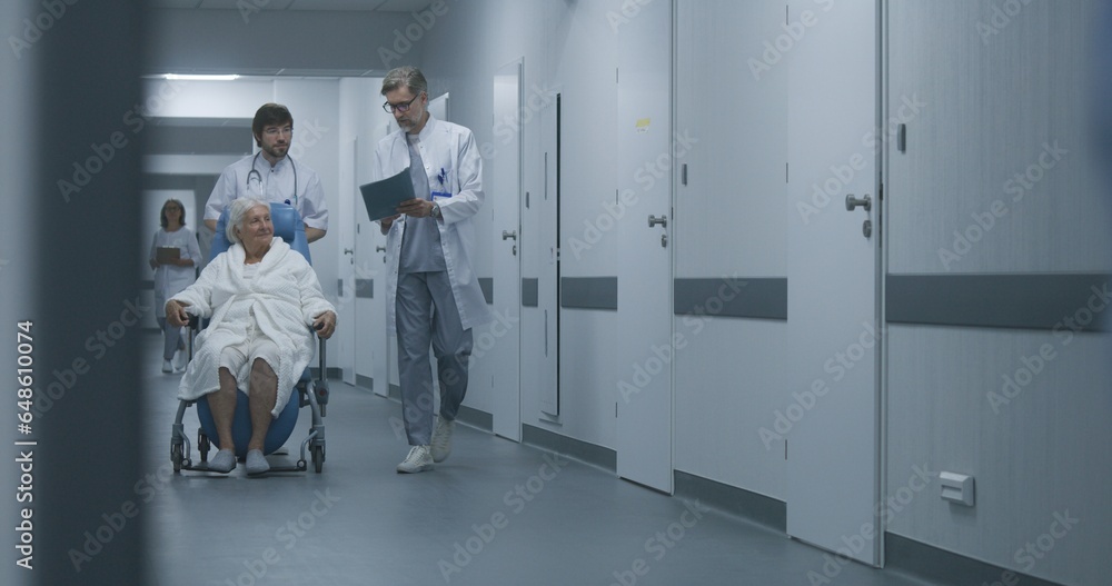 Back view of doctors pushing transfer wheelchair with patient walking ...