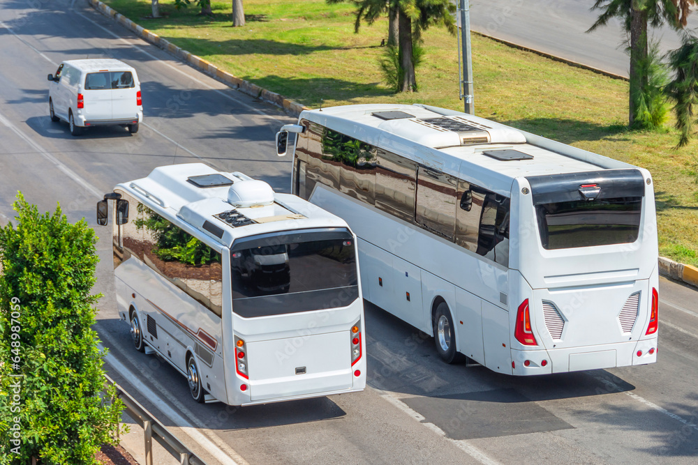 Two white buses, a large and a small one, travel opposite each other ...