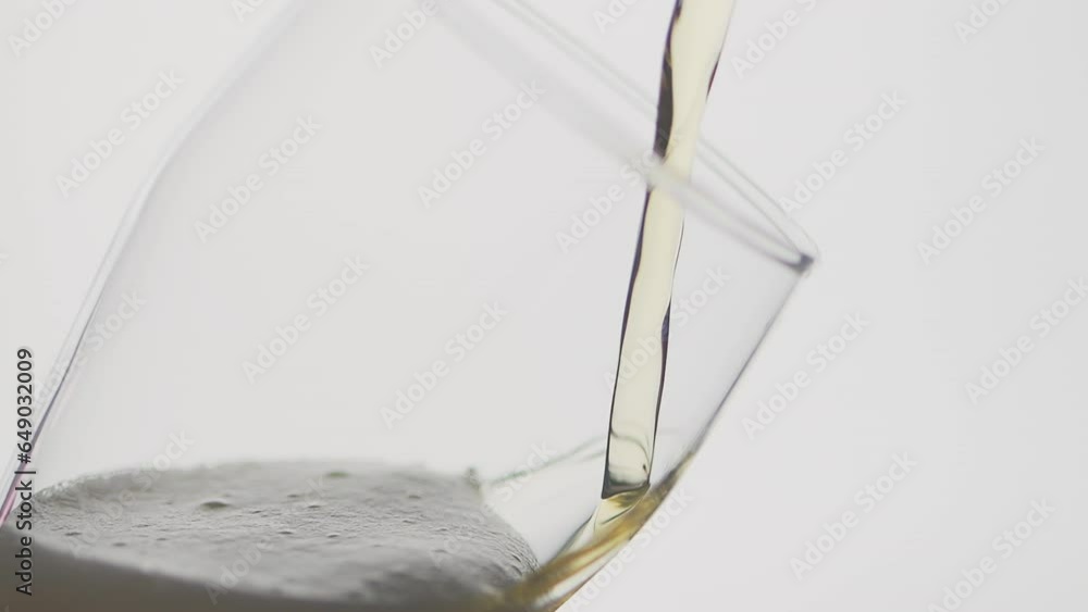 Foamy beer is poured into a tilted glass on a light white background, a ...