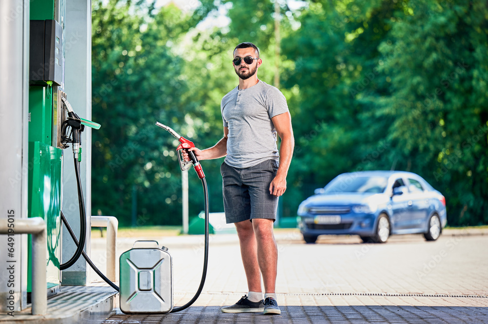 Handsome driver refueling canister with gasoline at modern gas station ...