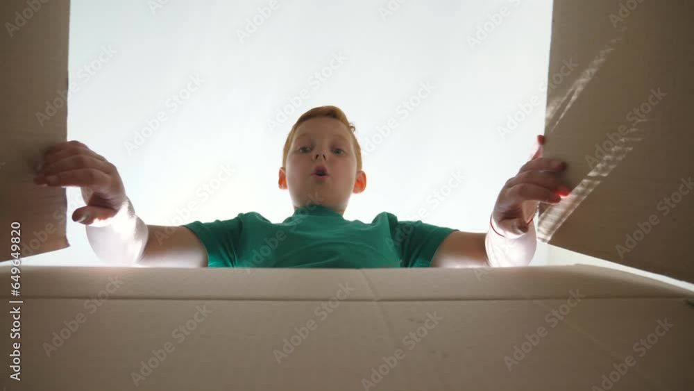 Small red-haired boy looking in parcel box with positive emotions and ...