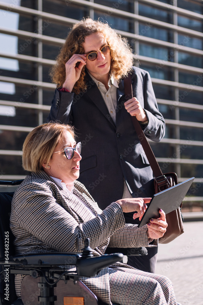 woman using wheelchair showing tablet to a business man in front of ...