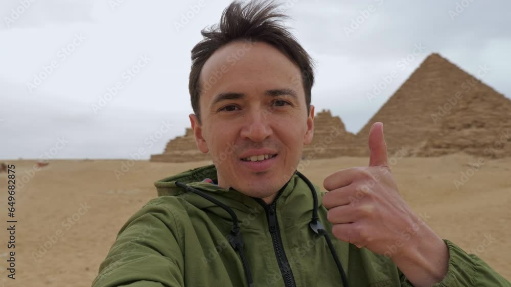 Young man takes selfie near ancient pyramids, smiling. Guy is ...