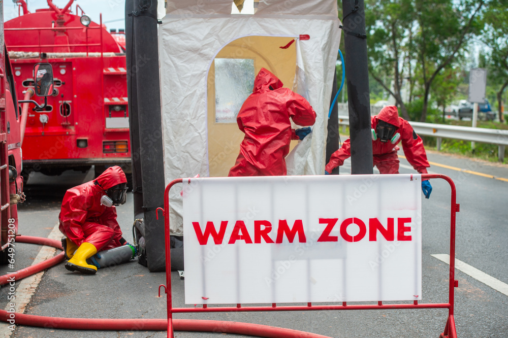 A warm zone sign, background with rescuers wearing red hazmat suits ...